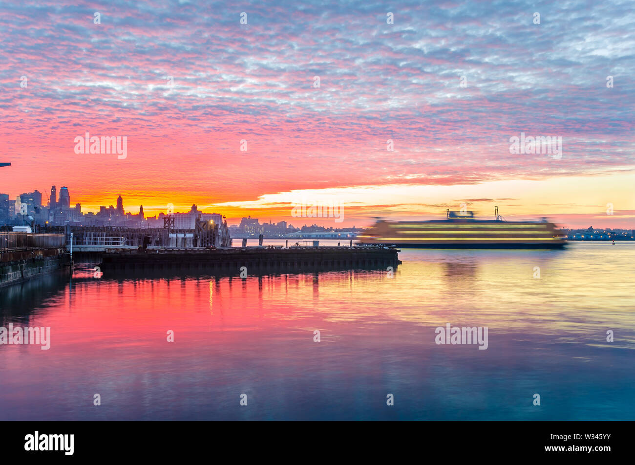 Stunning sunrise over Manhattan ferry terminal with a ferry leaving the ...