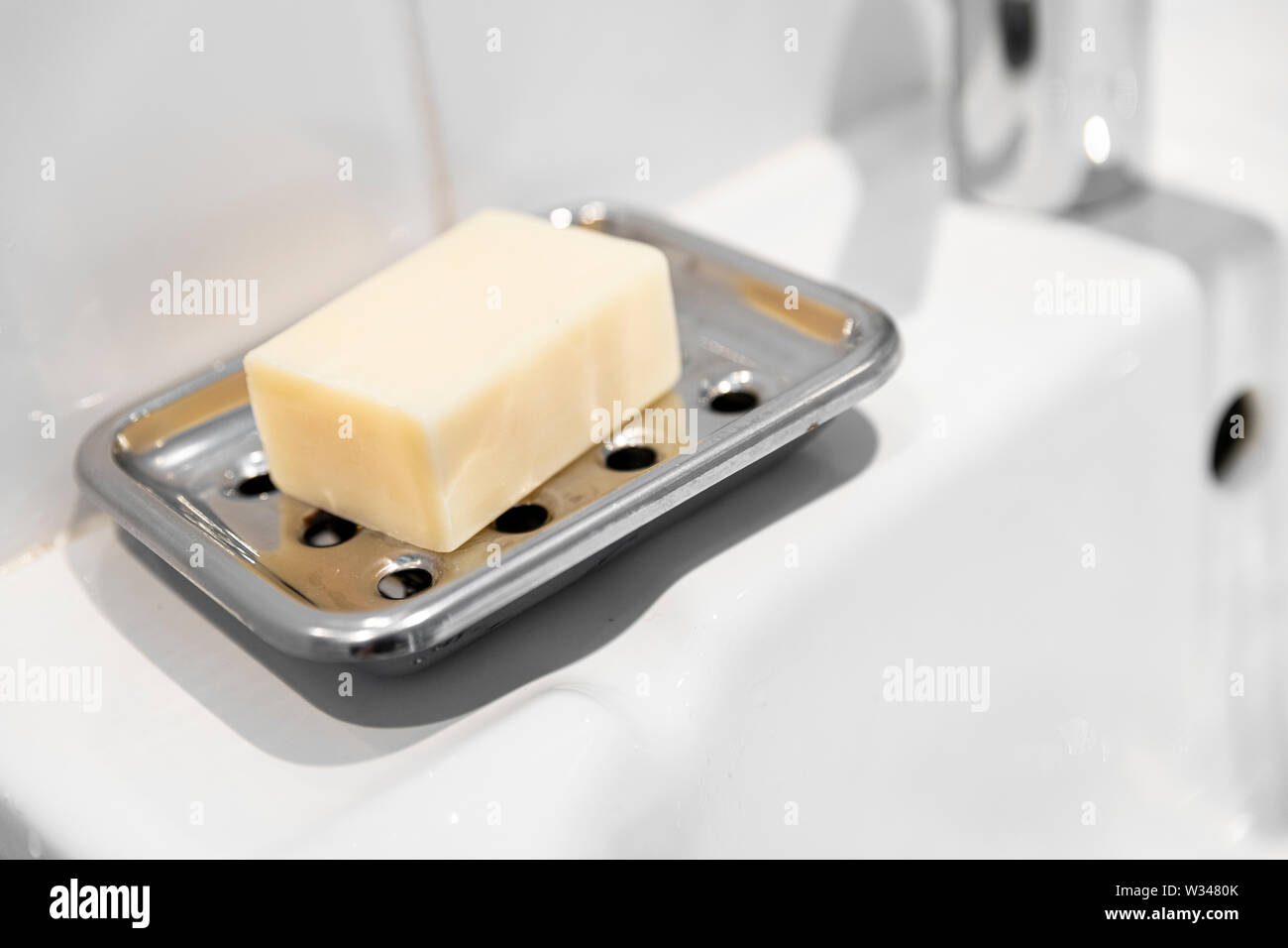 Bar of soap on a stainless steel dish on a white bathroom sink. A bar ...