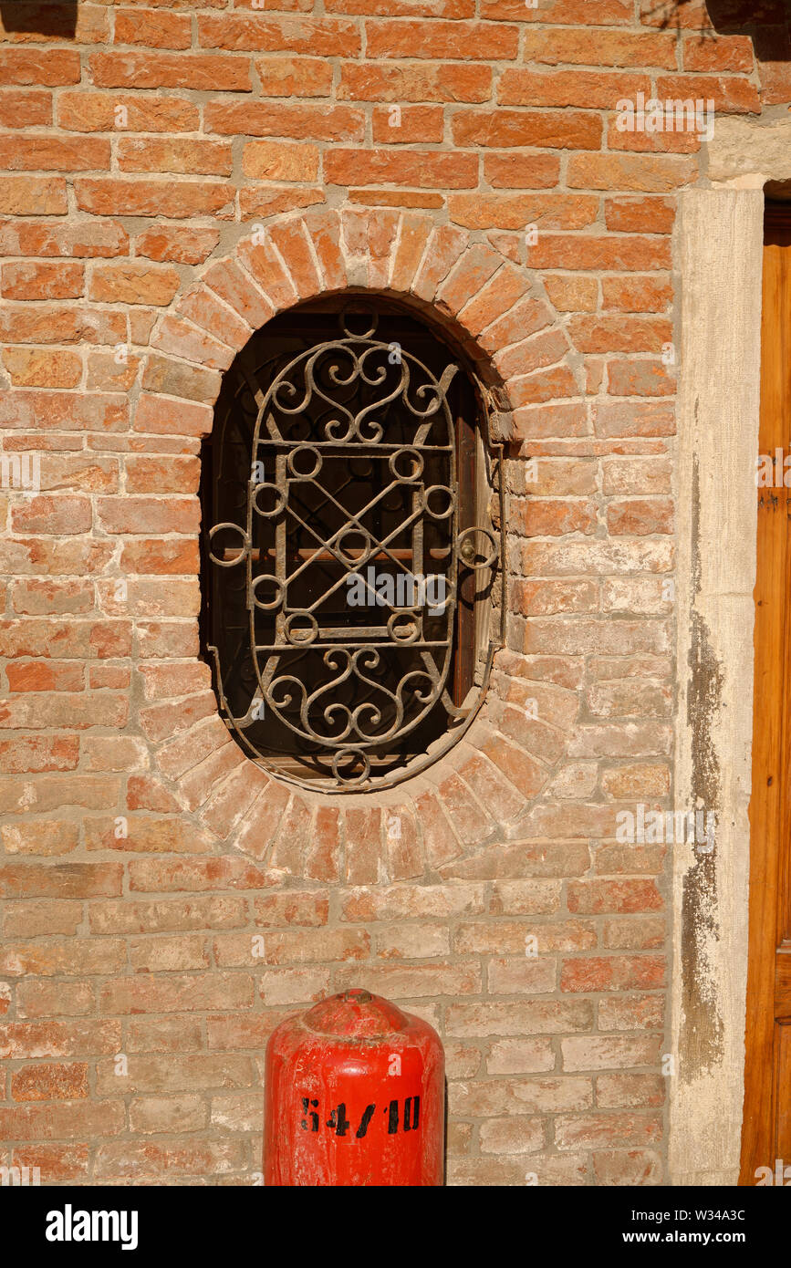 Portait oval shaped brick window with ornate ironwork security grill ...