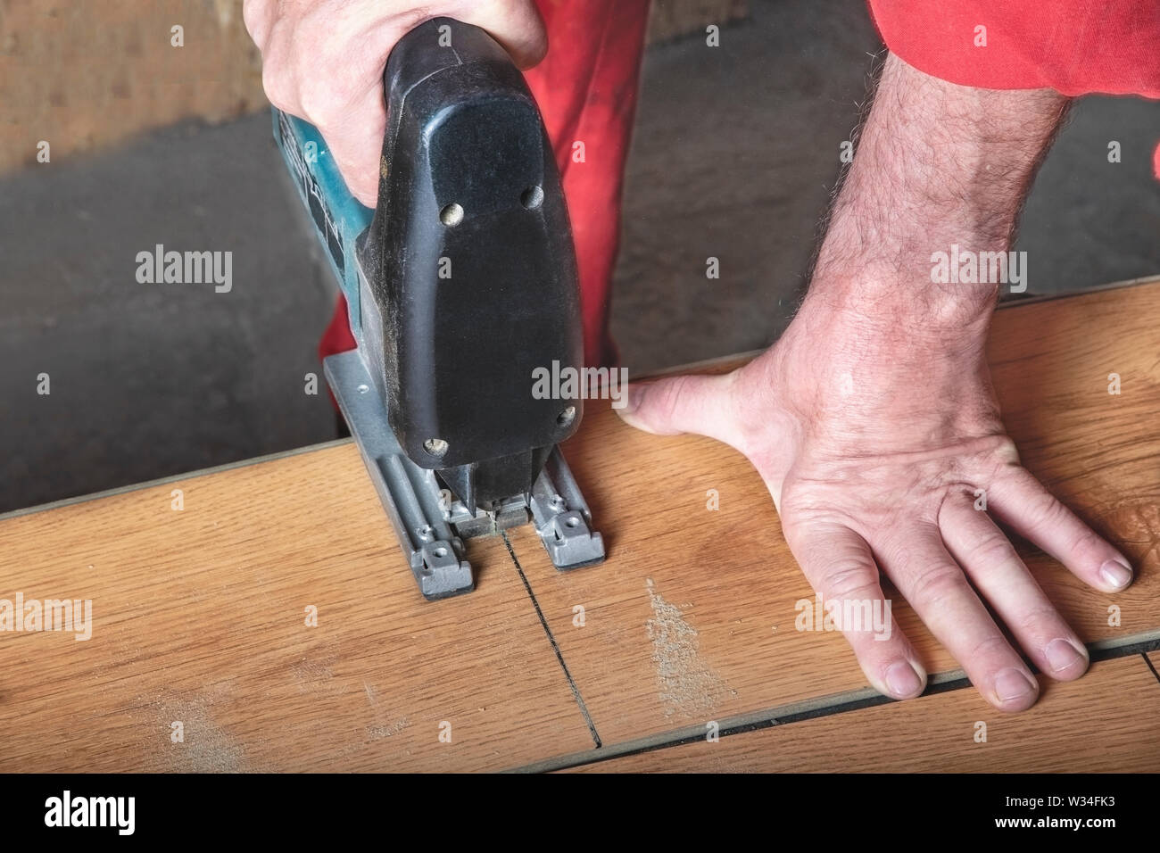 A worker in a red jumpsuit cuts a laminate with a jigsaw by marking ...