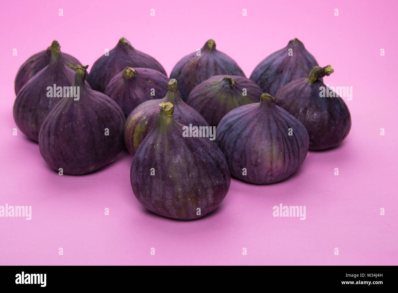 12 beautiful ripe purple figs are on a purple pink table. Several ...