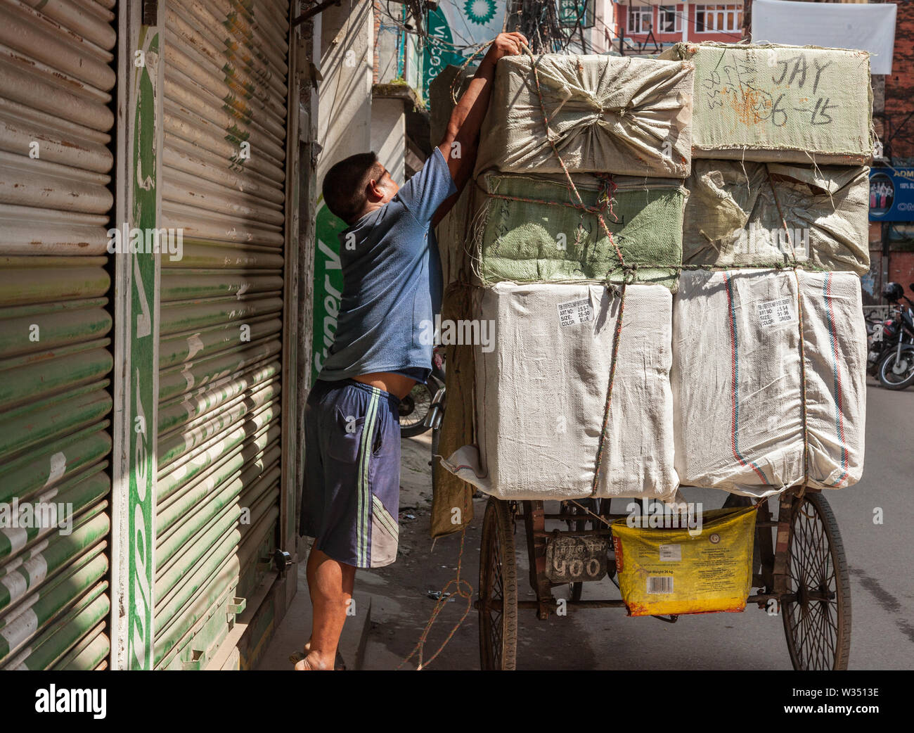Man tying bundles of goods to a tricycle cart on a street in Kathmandu ...