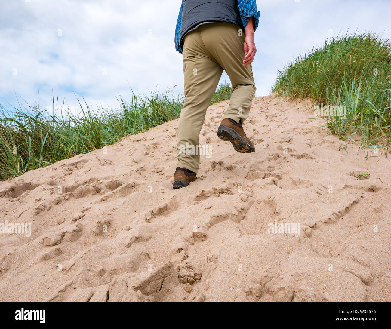 Senior man trudging up steep sand dune slope, Aberlady Nature Reserve ...