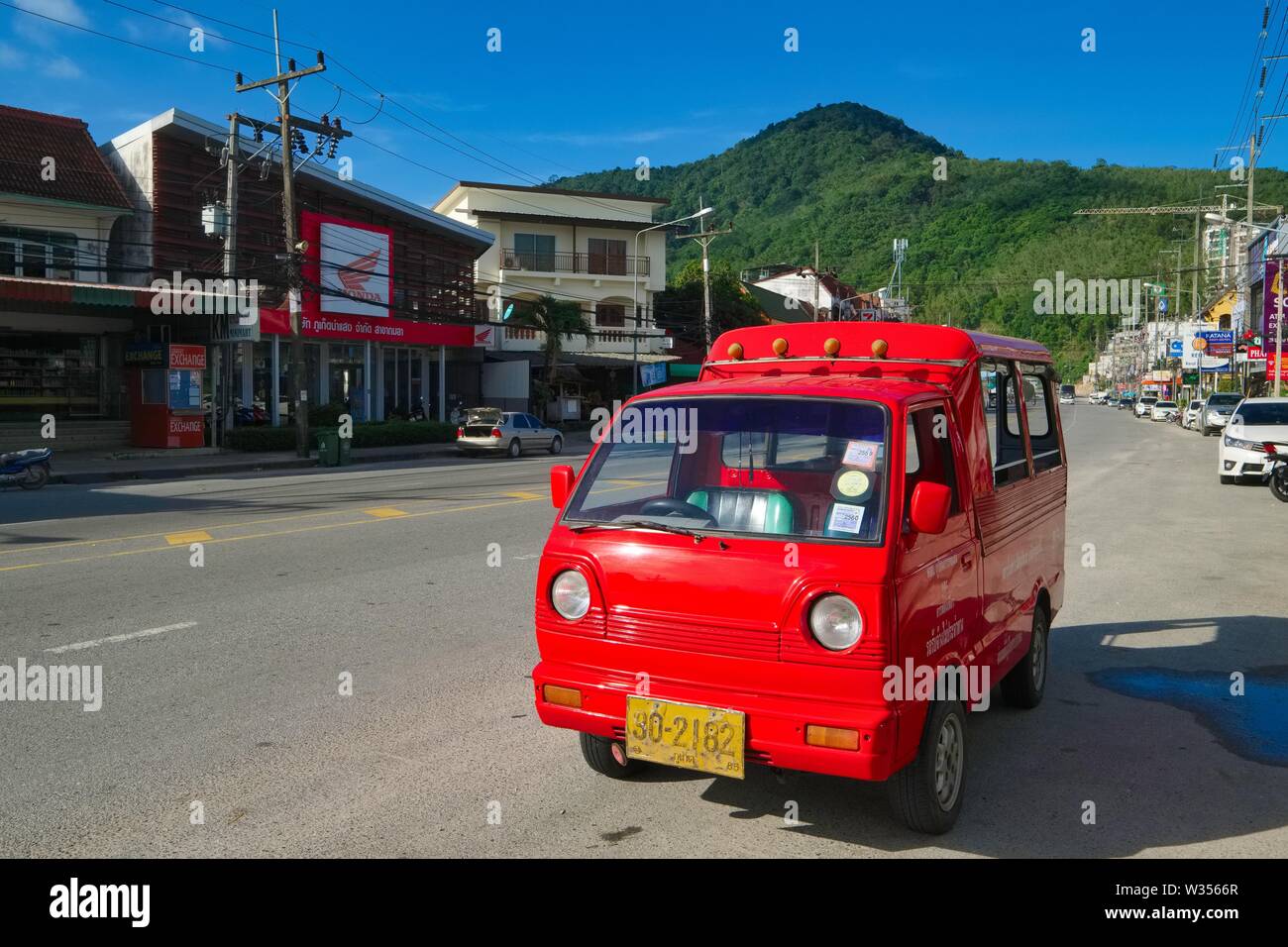 A red tuk-tuk, a four-wheeled local taxi, is parked in the main road ...