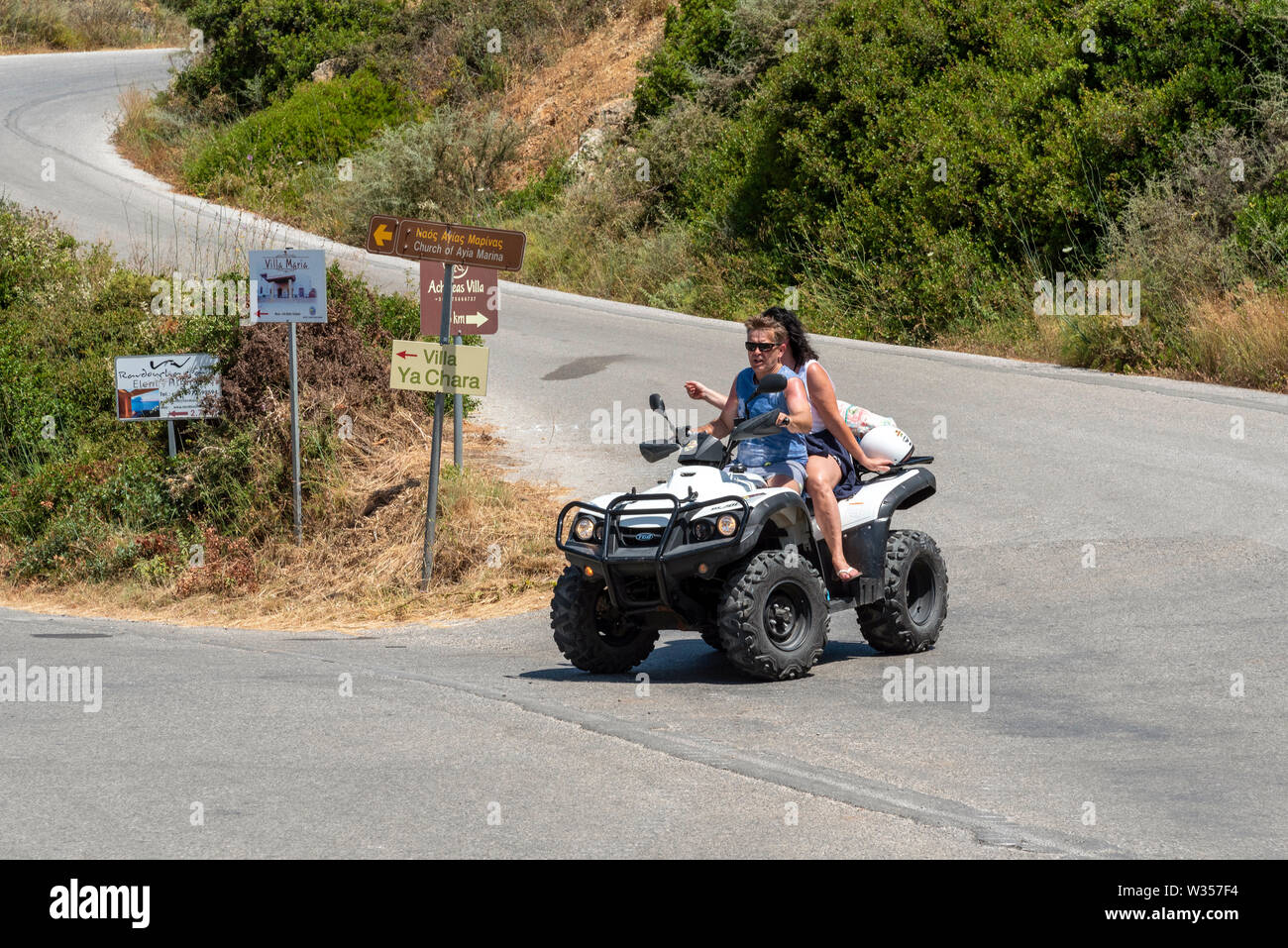 Crete, Greece. June 2019. Couple riding a quad bike on a country lane ...