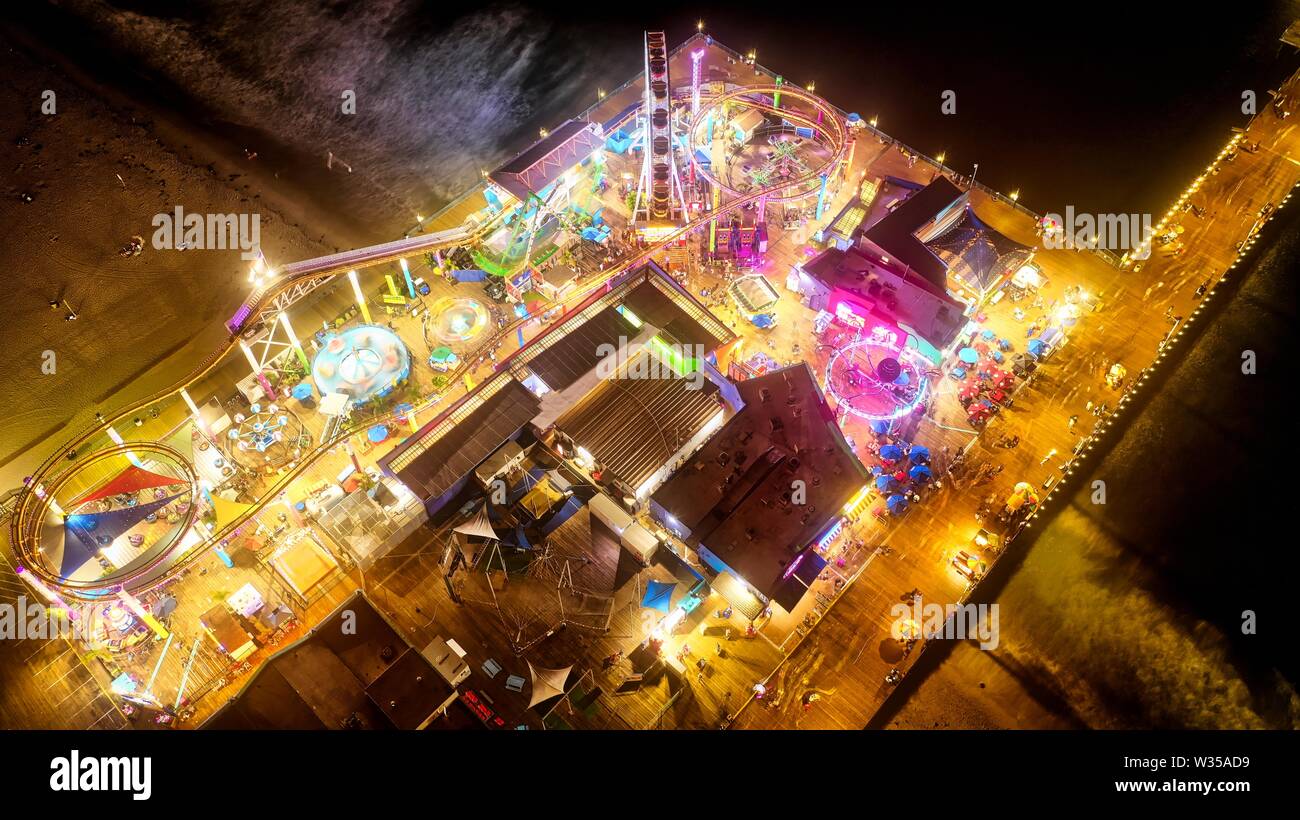 Aerial shot of a carnival at an attraction park near the beach at night ...