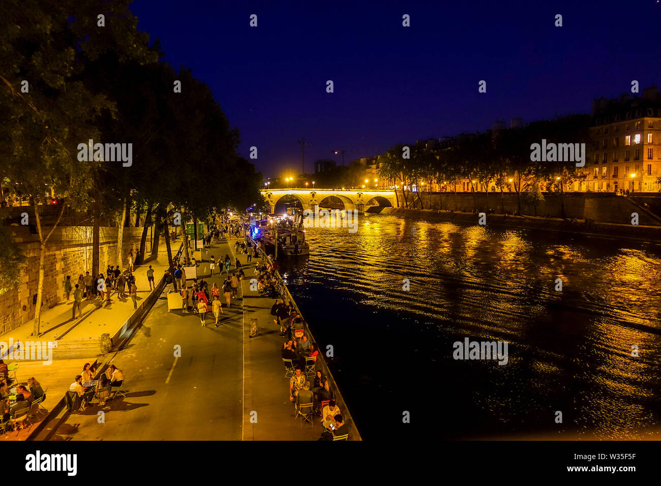 People walk the quai near Pont Marie bridge illuminated at night ile saint louis, at the Seine ...