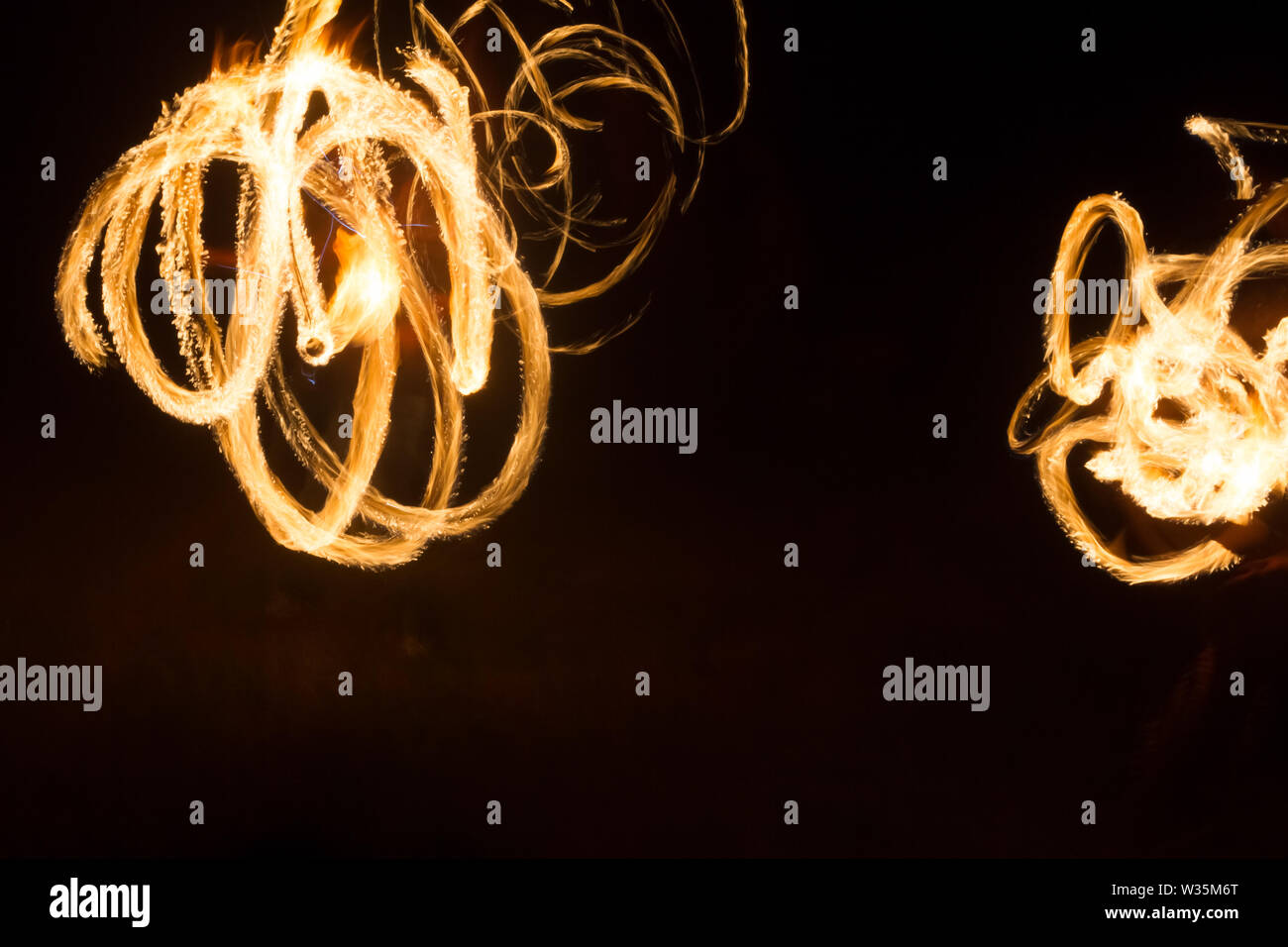 An artist shows a fire show at night spinning torches, circles of fire ...