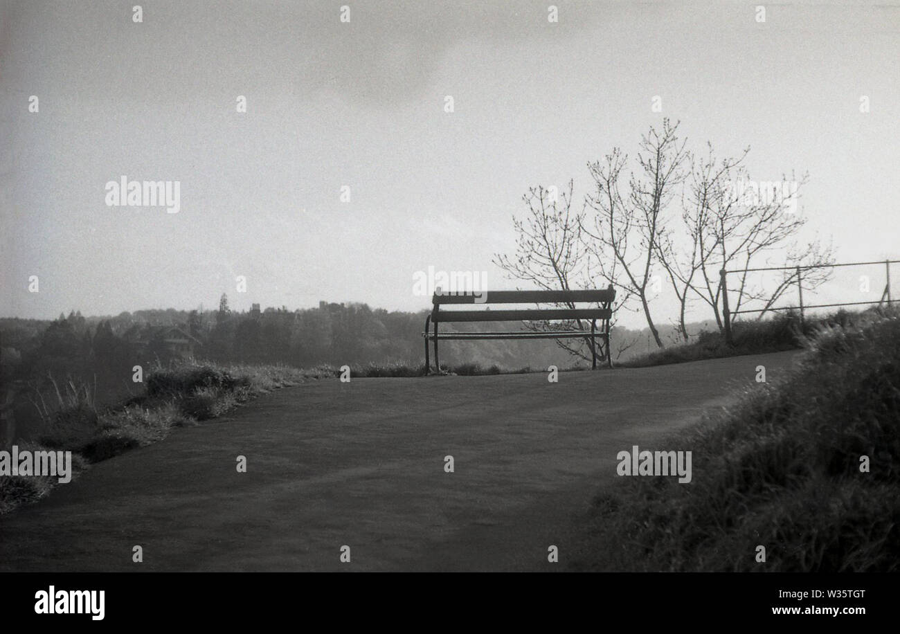 1950s, historical, a wooden bench on a hill-side path overlooking ...