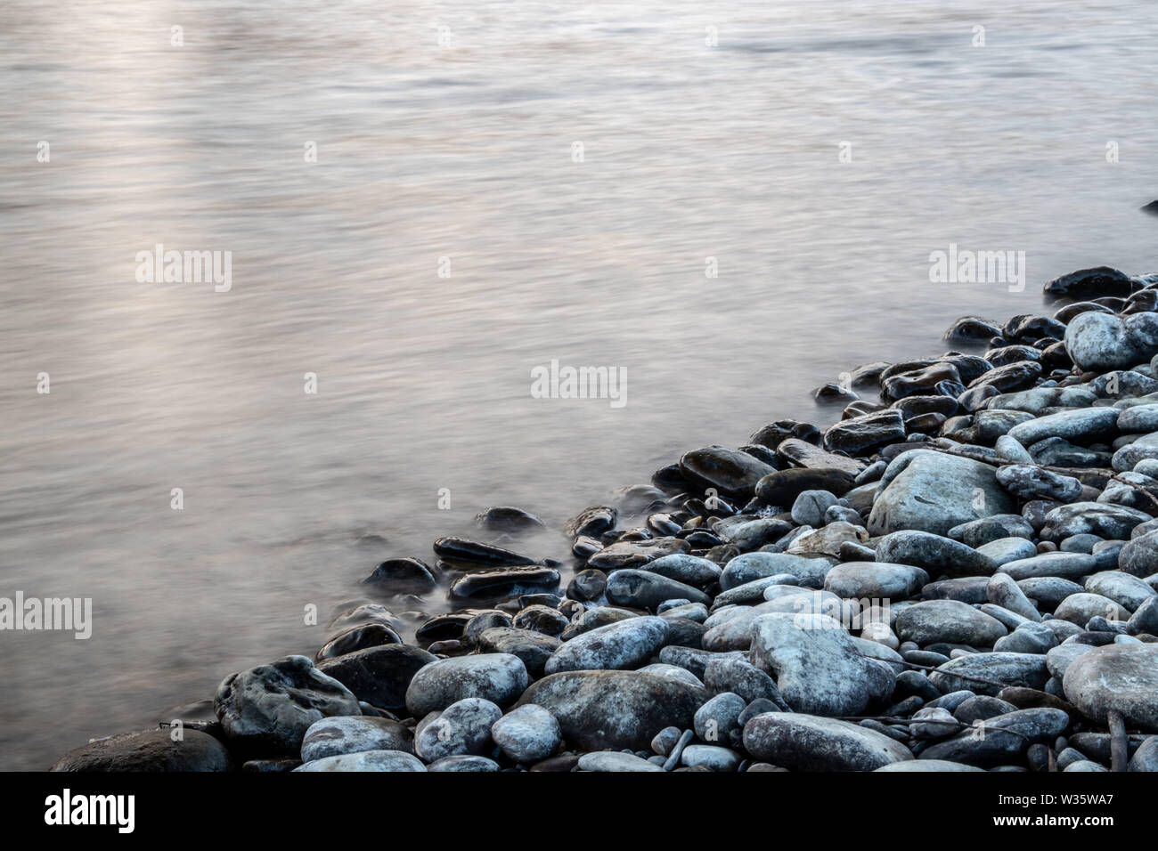 Shore stones covered in water with space on the left for text Stock ...