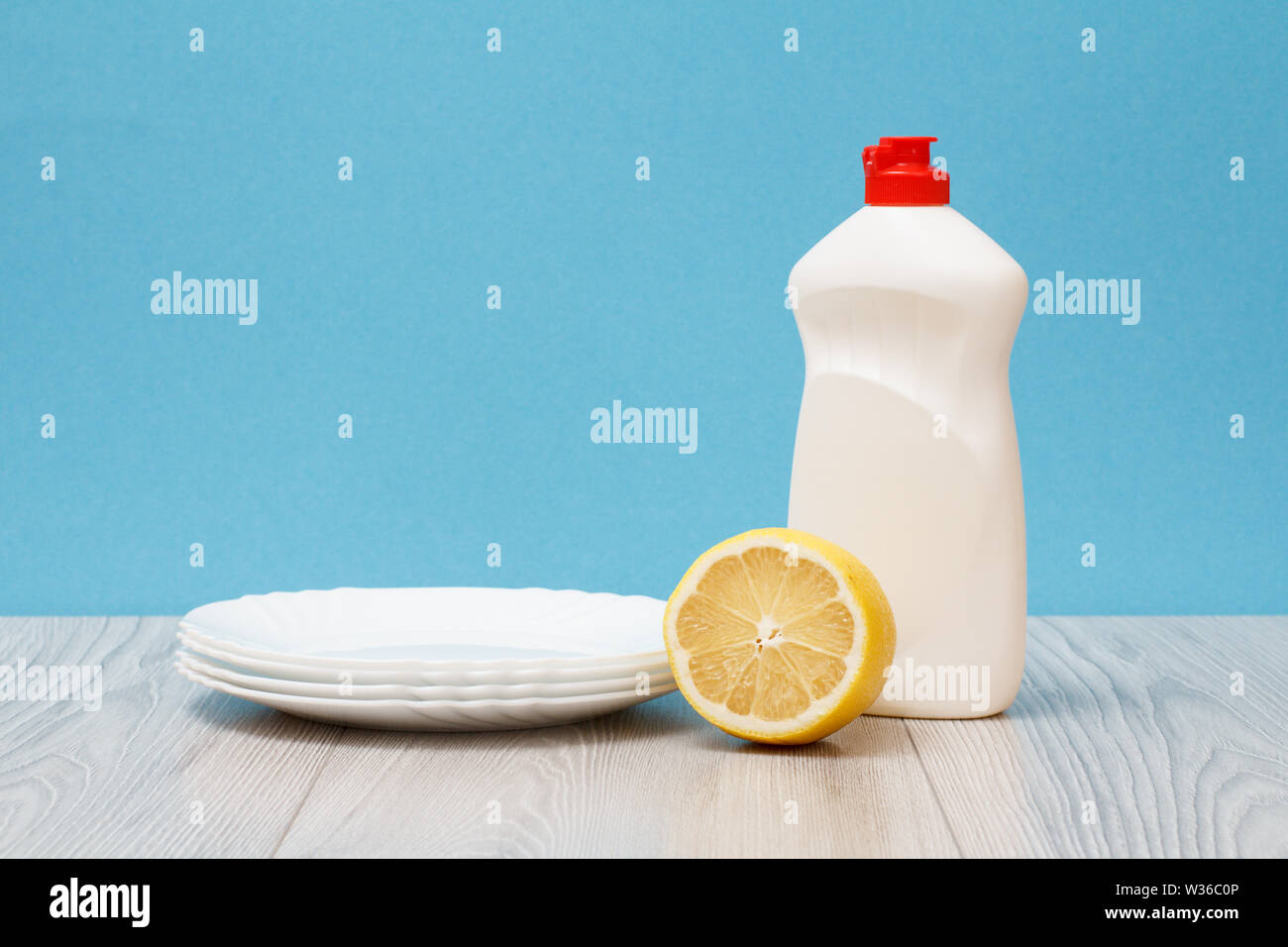 Plastic bottle of dishwashing liquid, clean plates and lemon on wooden ...