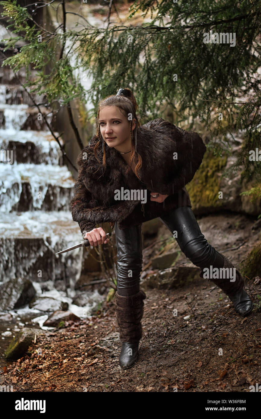 girl with a dagger with a dagger near a waterfall in a forest in the ...