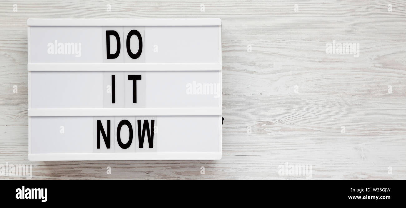 'Do it now' words on a modern board on a white wooden surface. Flat lay ...