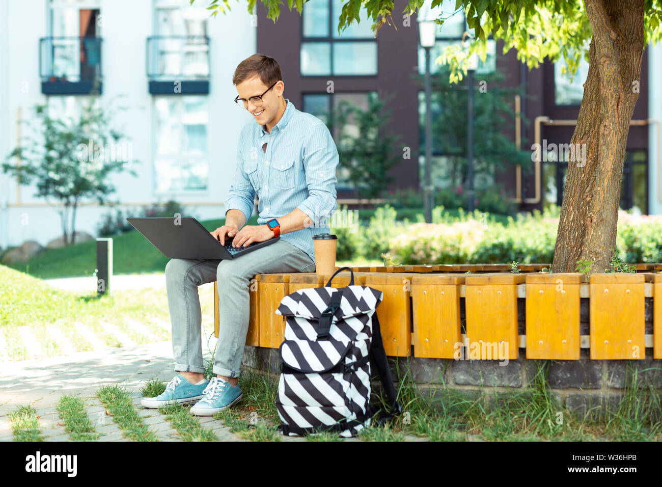 Man wearing smart watch working on laptop sitting near tree Stock Photo ...