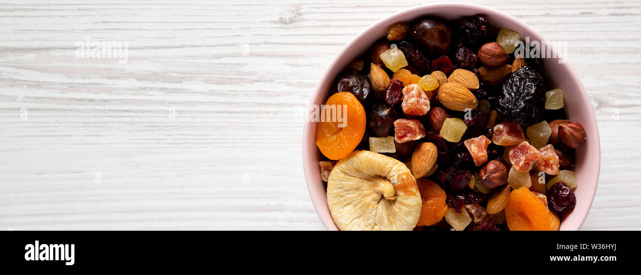 Dried fruits and nuts in a pink bowl over white wooden background ...