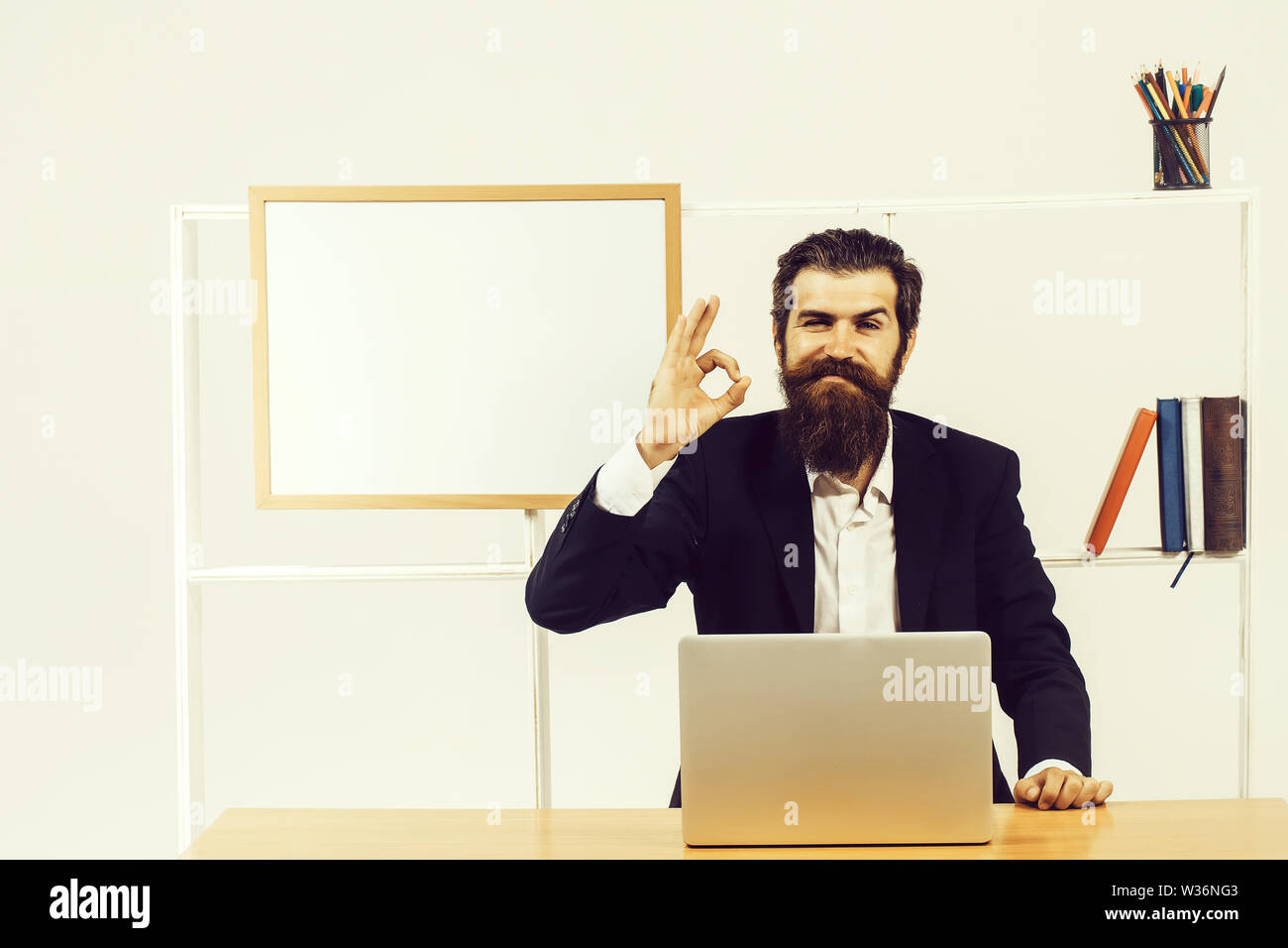 Smiling bearded employee in black suit showing OK sign by hand sitting ...