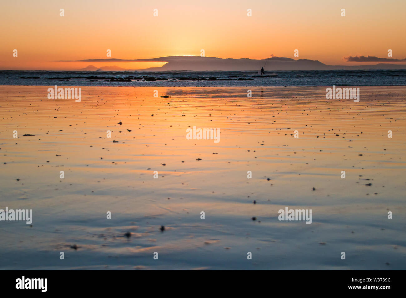 Orange beach sunset with fisherman silhouette and light reflecting off ...