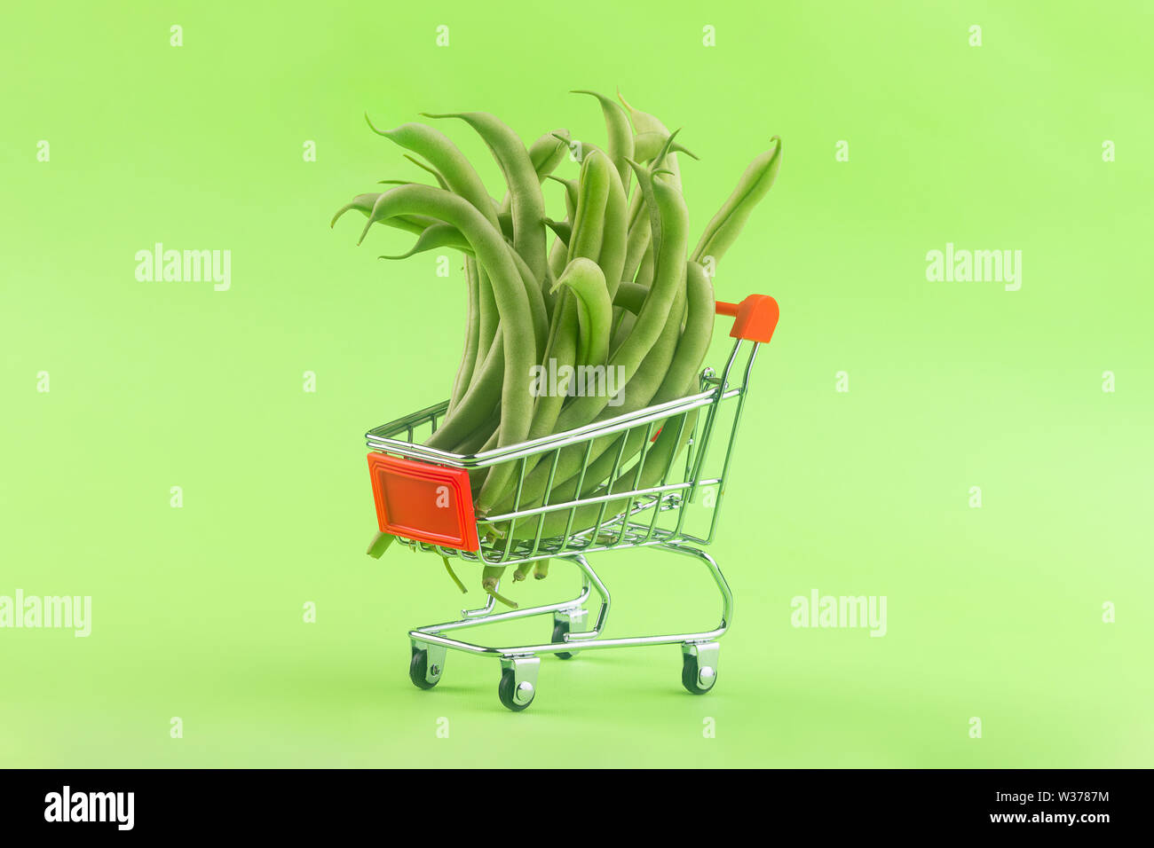green beans in a shopping cart over green background, buying vegetarian ...