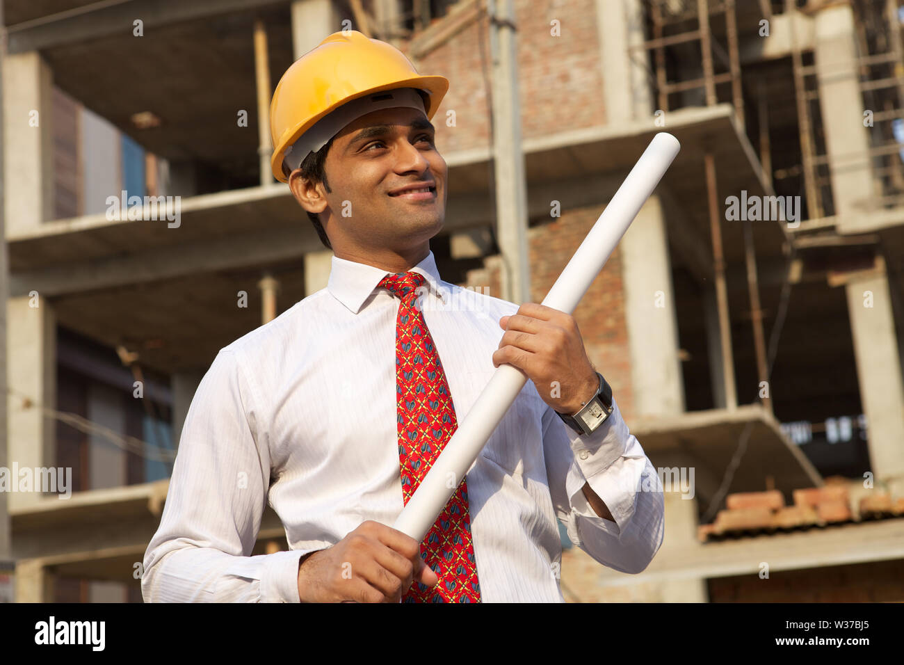 Architect at construction site and holding blueprint Stock Photo - Alamy