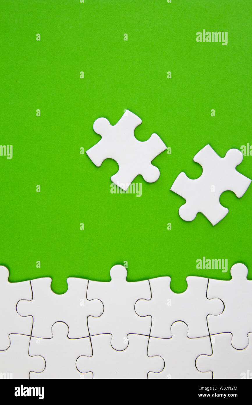 White jigsaw puzzle pieces on green background with negative space ...