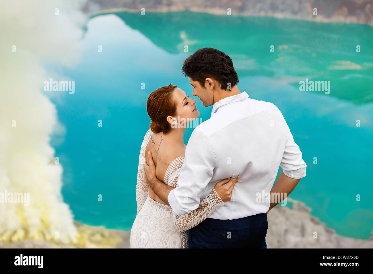 Bride and groom hugging against the backdrop of a green lake and ...