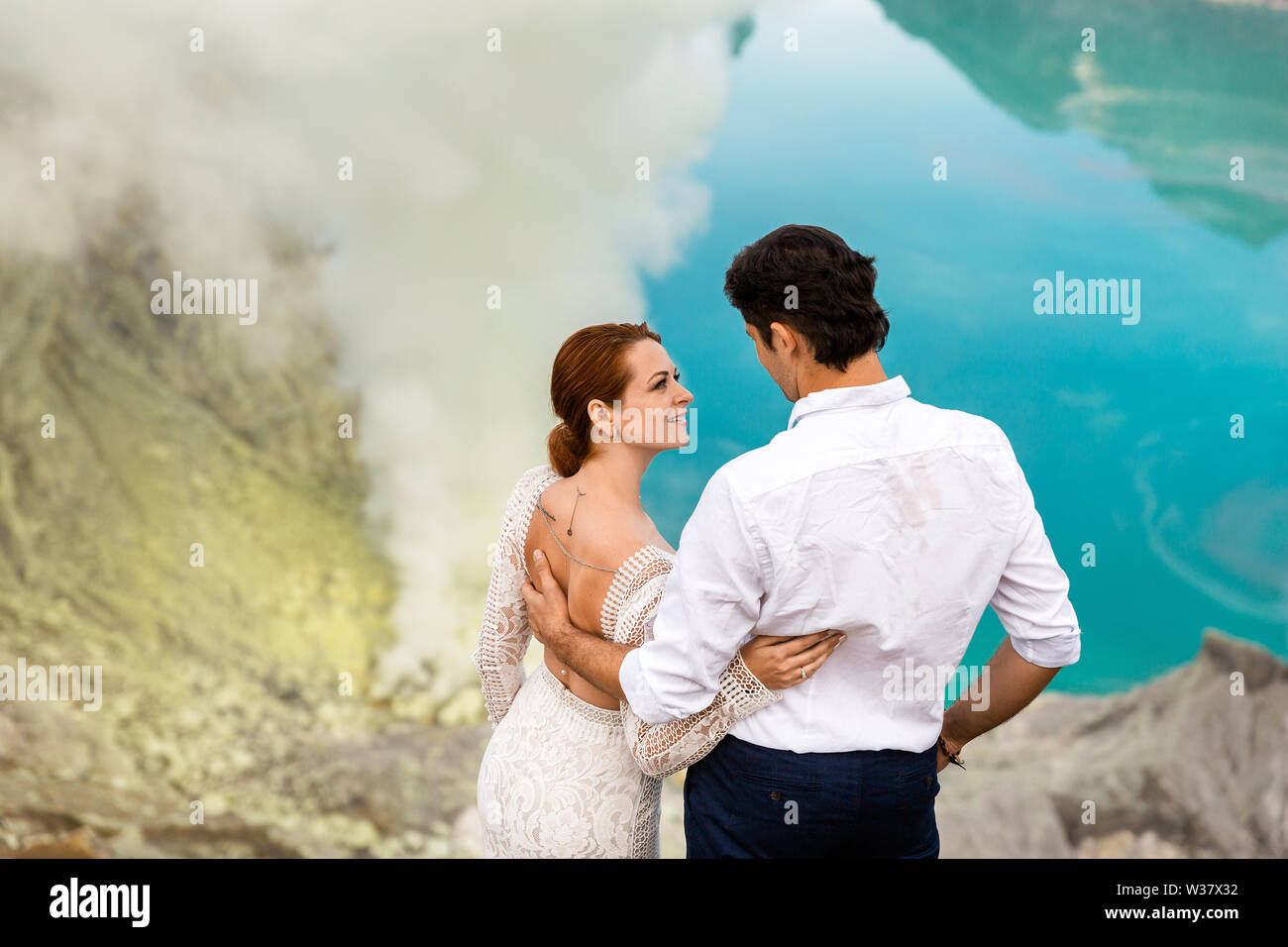 Bride and groom hugging against the backdrop of a green lake and ...