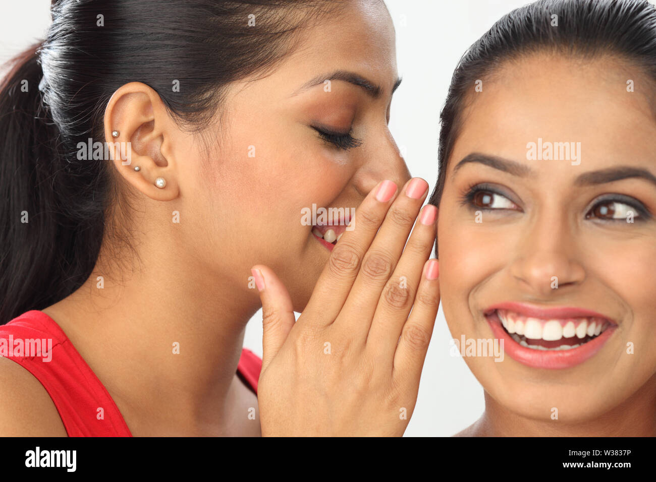 Woman whispering into her friend's ear Stock Photo - Alamy