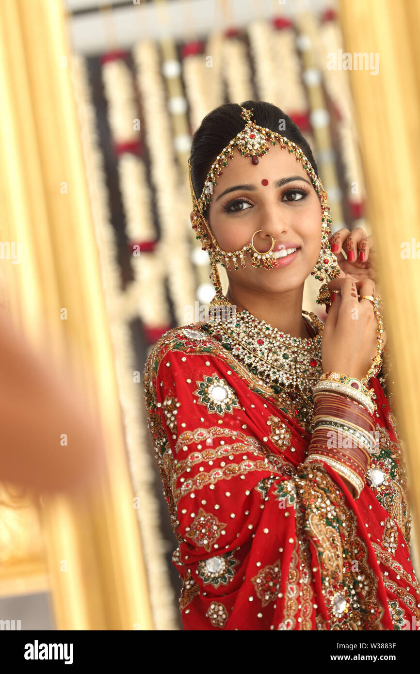 Indian bride adjusting her earring looking into mirror Stock Photo - Alamy