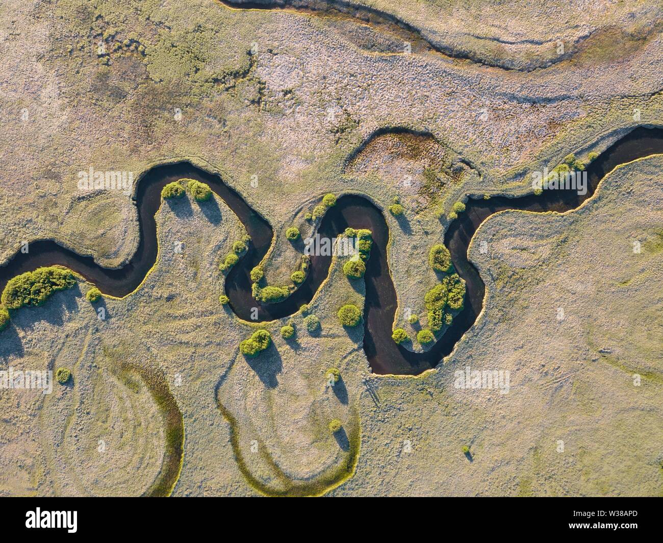 A stream meanders through a green valley, with natural twists and ...