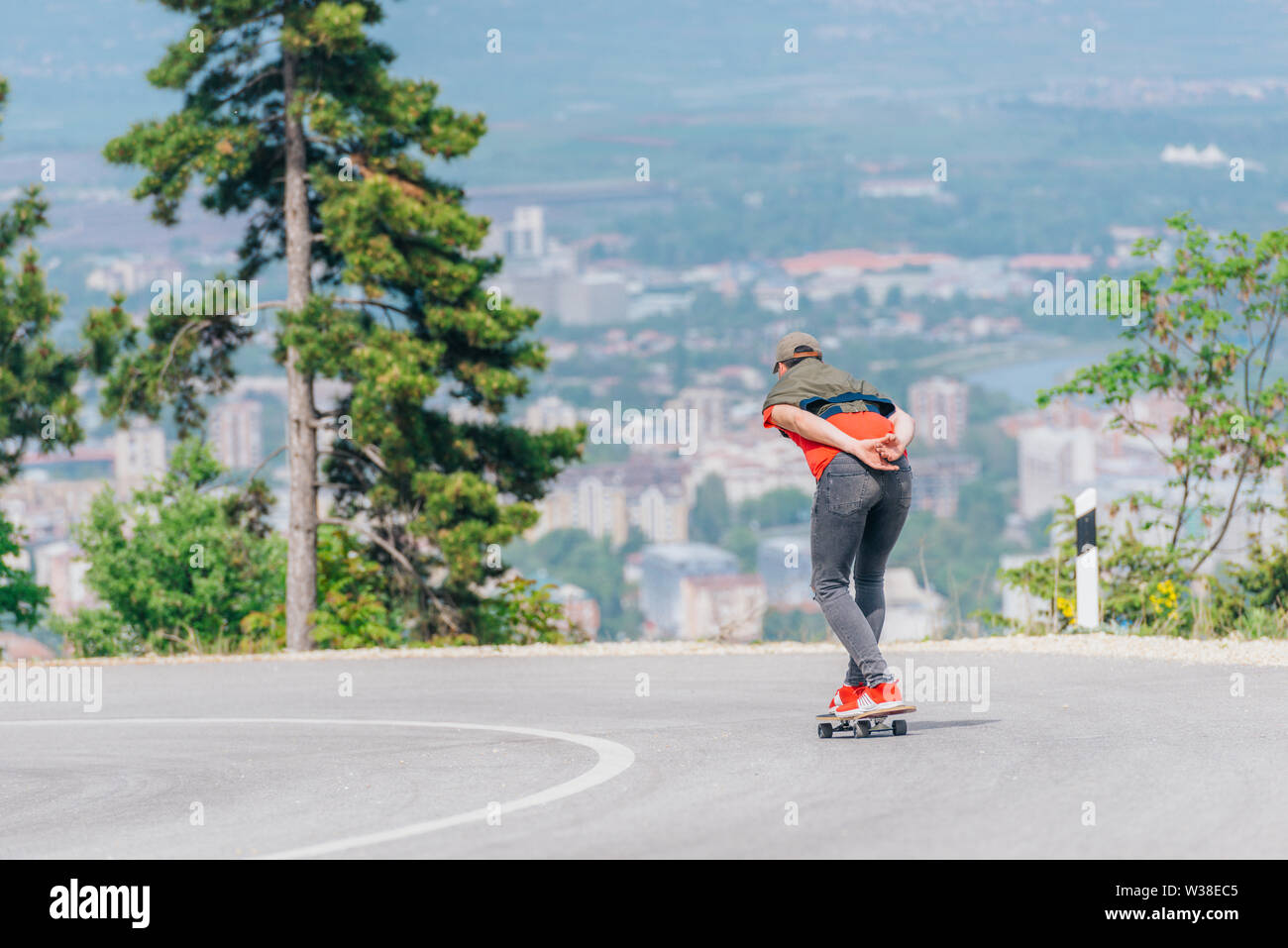 Tall athlete riding his longboard fast and steady downhill while ...