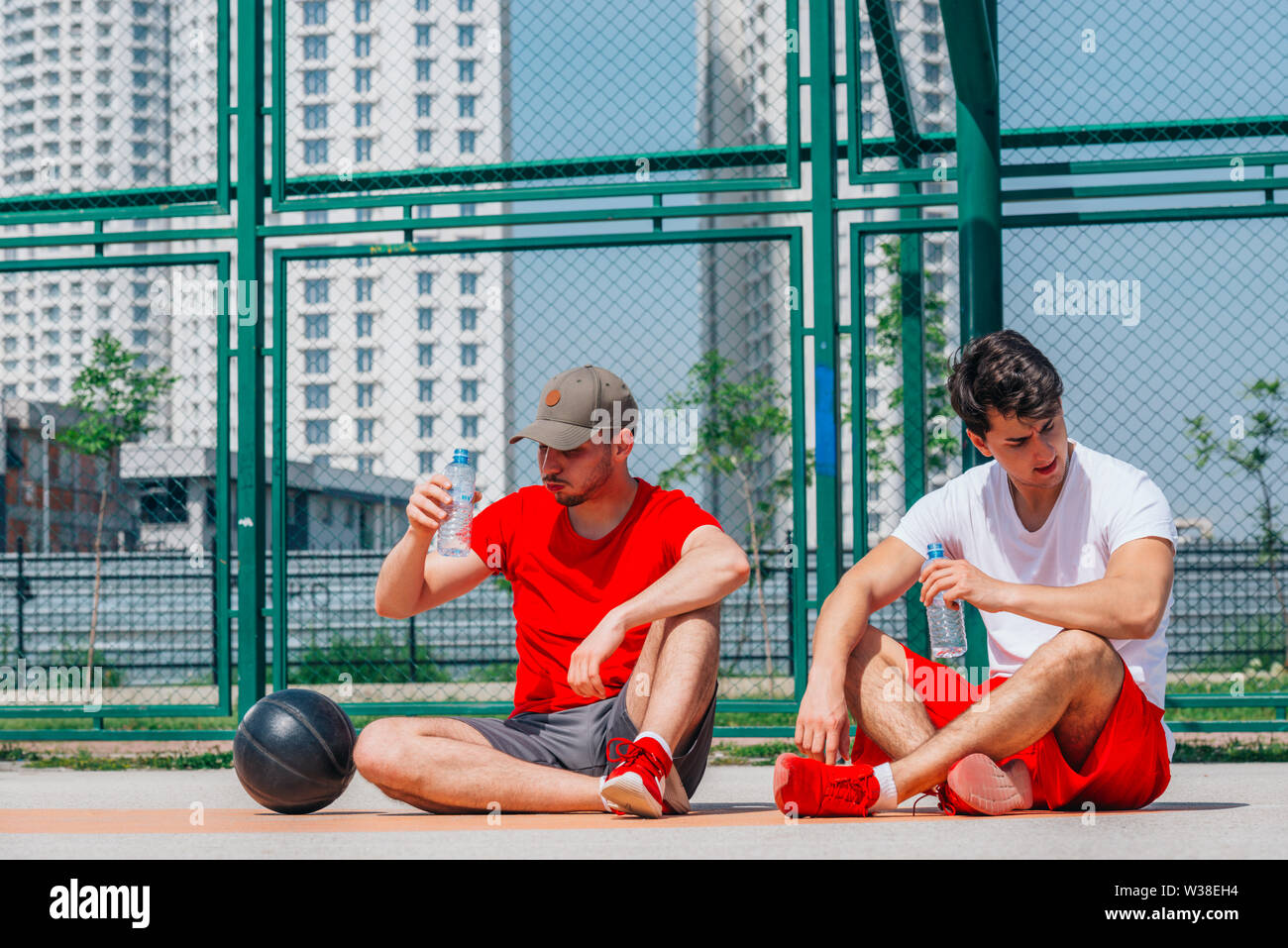 Two basketball players having some rest sitting on the court after an ...