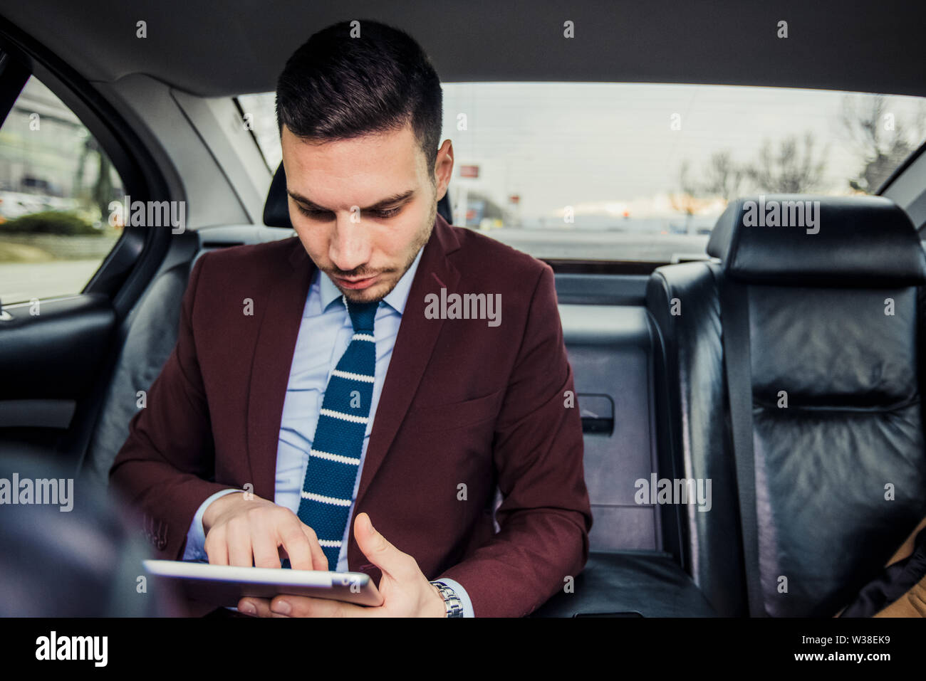 Urban businessman is looking at his tablet while driving in a limo ...