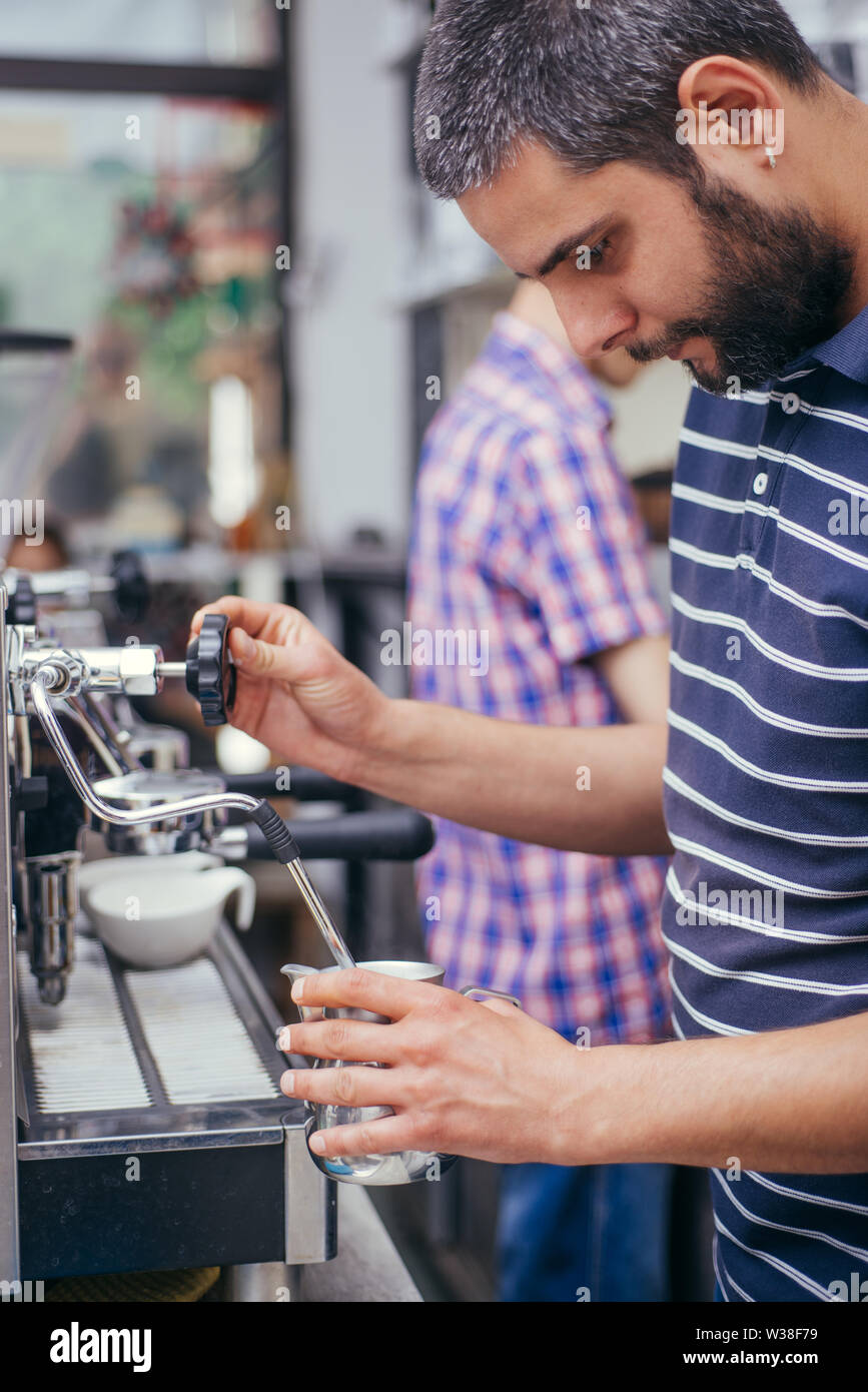 Barista in coffee bar preparing proper cappuccino pouring frothed milk ...