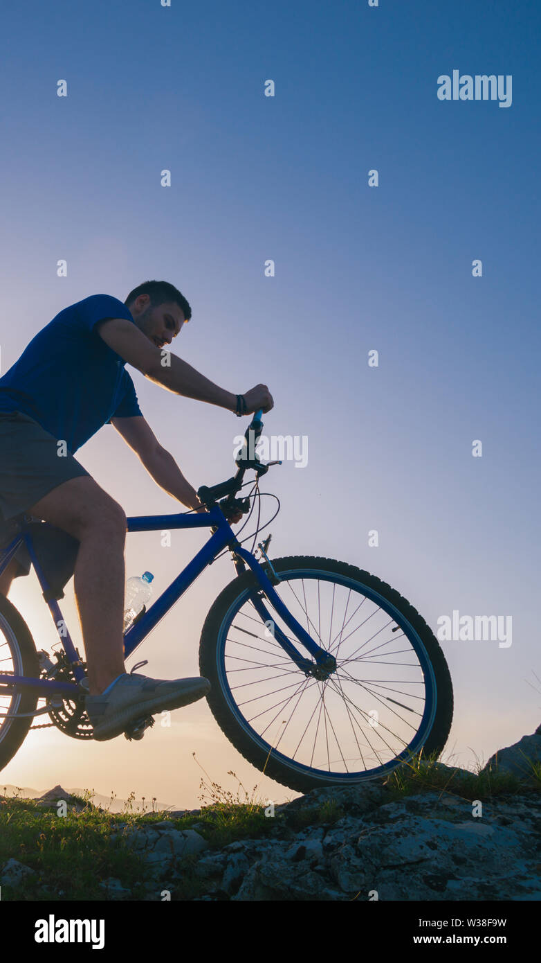 Strong fit male mountain biker performing stunts on rocky terrain on a ...