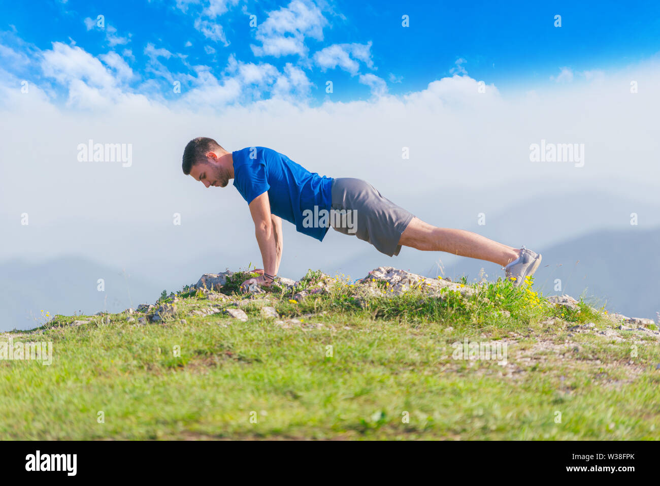 A young fit male athlete is doing push-ups outdoors on a cliff while ...