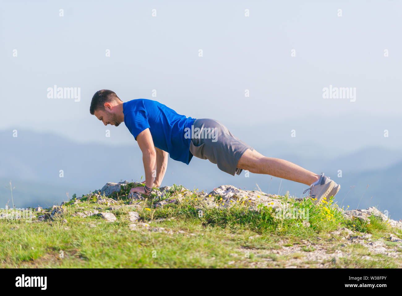 A young fit male athlete is doing push-ups outdoors on a cliff while ...