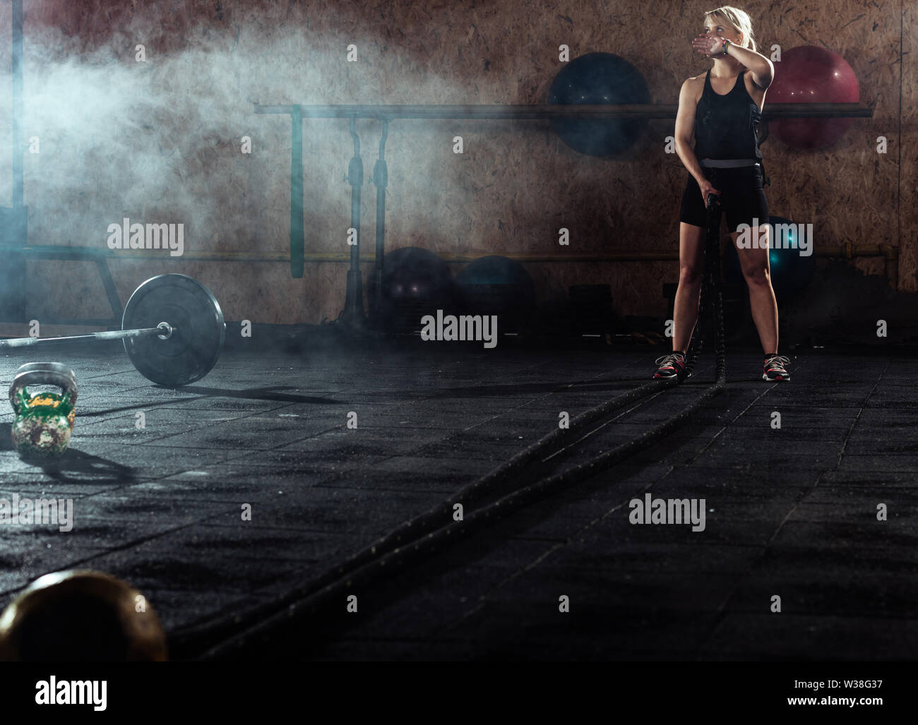 Attractive muscular woman working out with heavy ropes in crossfit ...