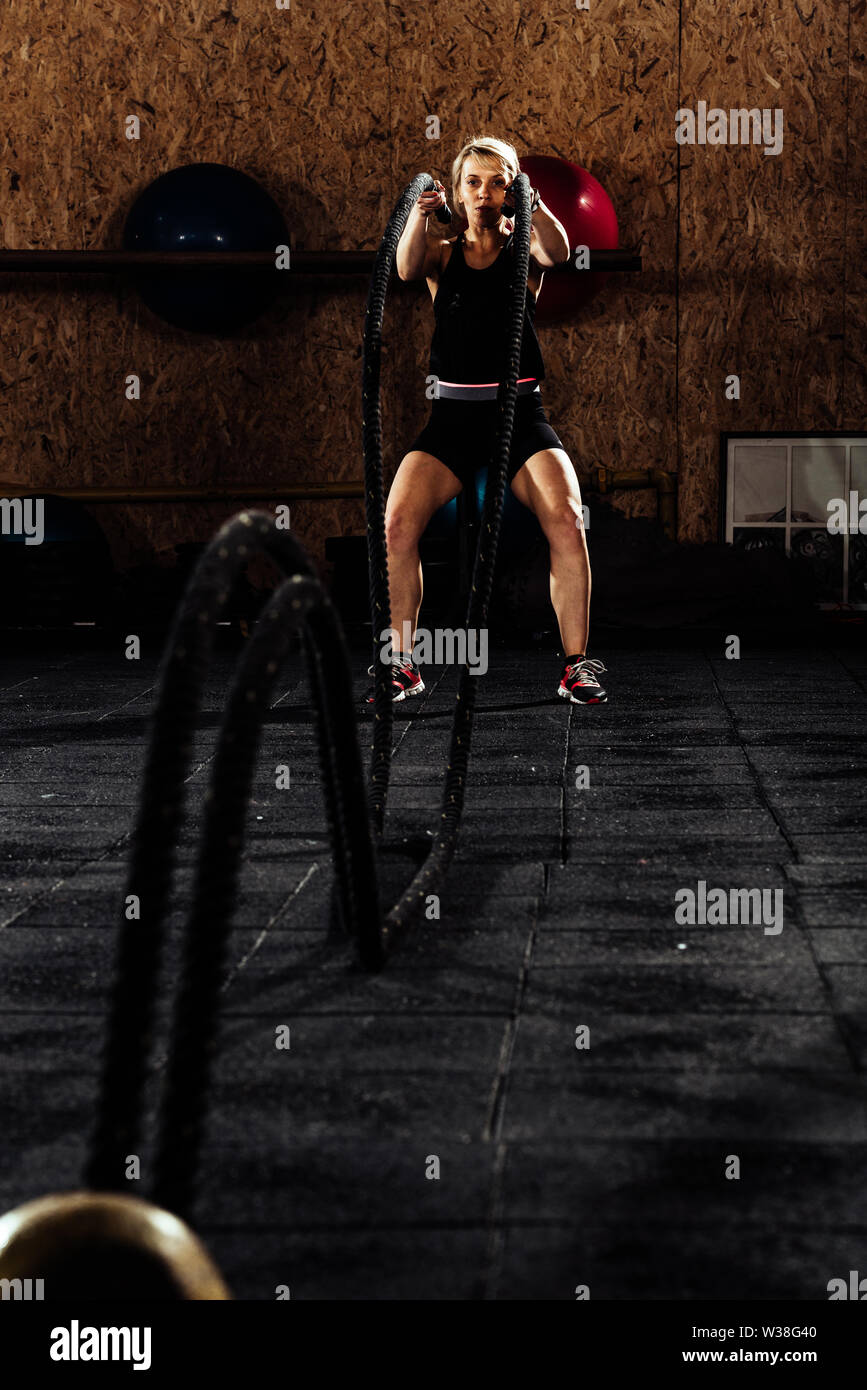 Female athlete making wave movement with battle rope during crossfit ...
