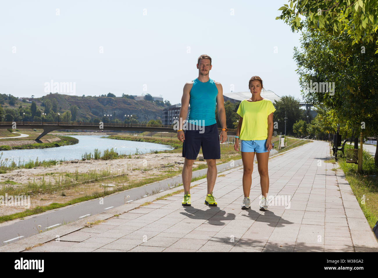 Shot of young man and woman running through the riverside track Stock ...