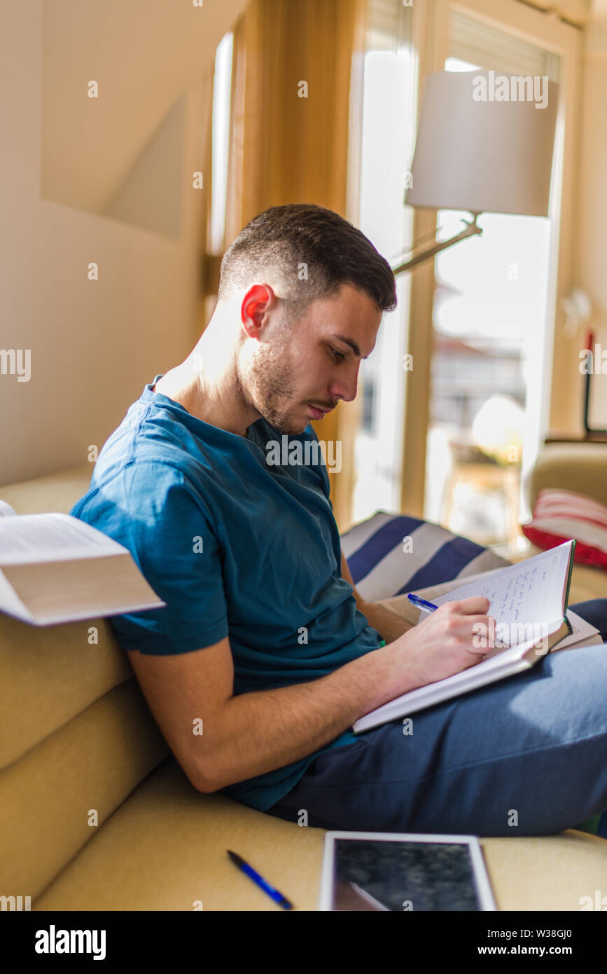 A handsome man is taking notes while learning from the book Stock Photo ...