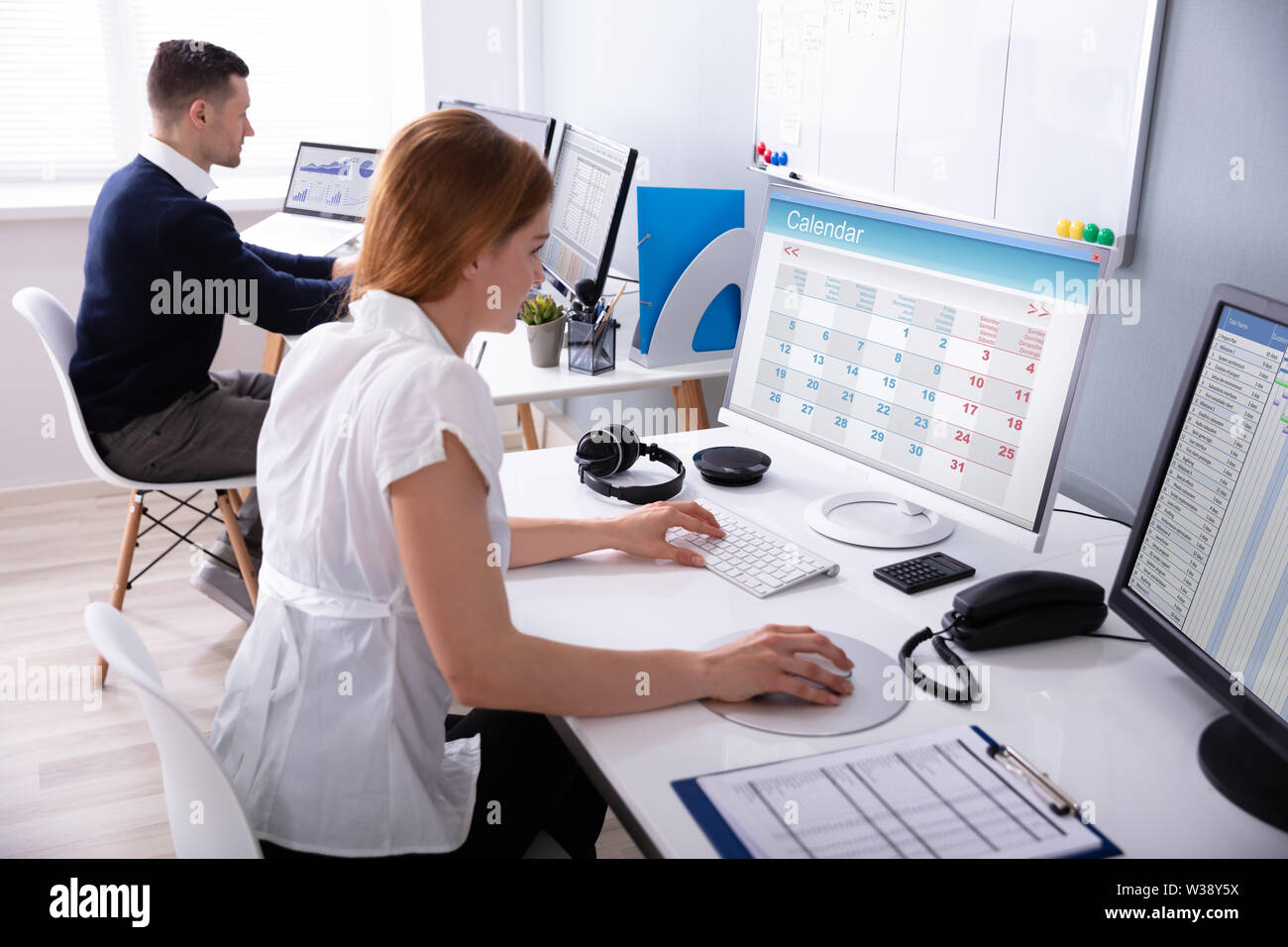 Businesswoman Looking At Calendar On Desktop Computer With Colleague ...