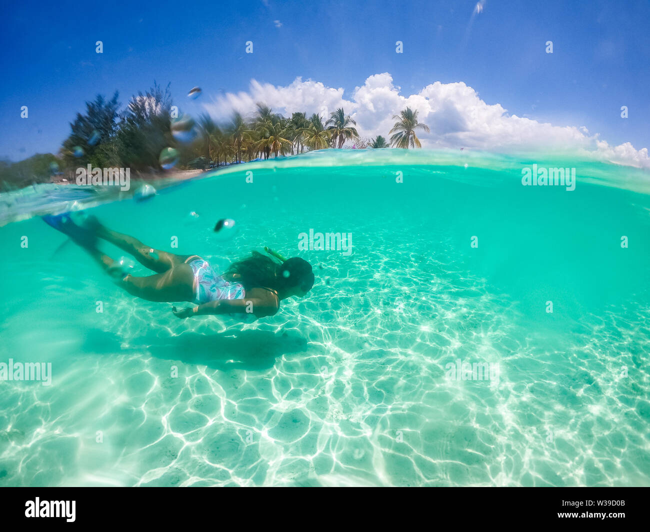 Woman swimming on a tropical beach with blue water and palm trees ...