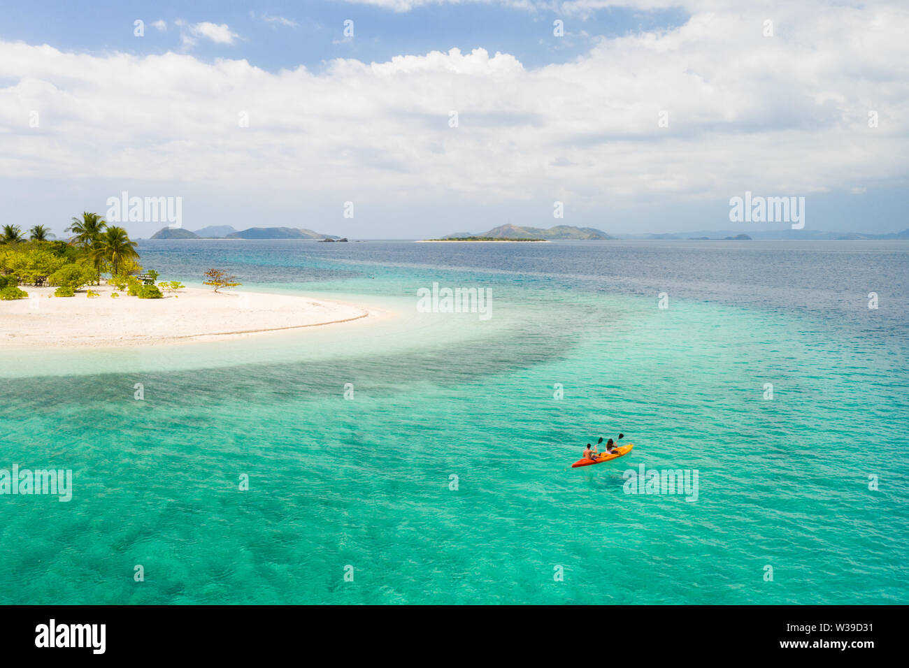 Couple kayaking on a tropical beach with blue water and palm trees ...