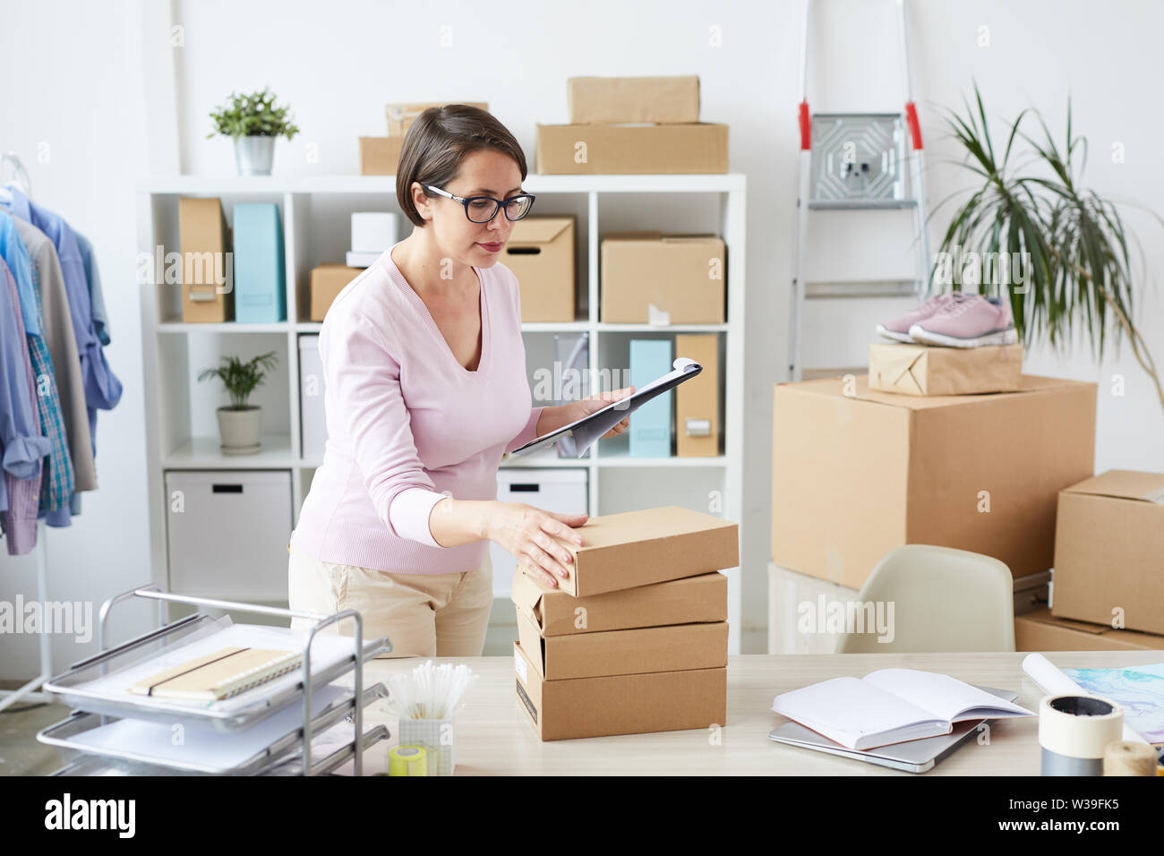 Young online shop manager with list of orders taking top box of stack ...