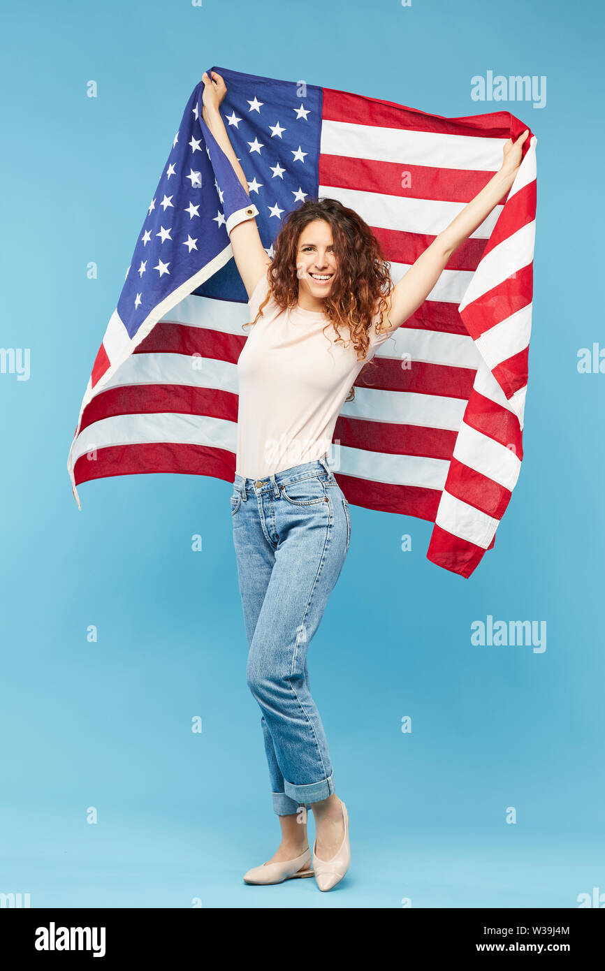 Young cheerful female with long dark curly hair holding flag of USA in ...
