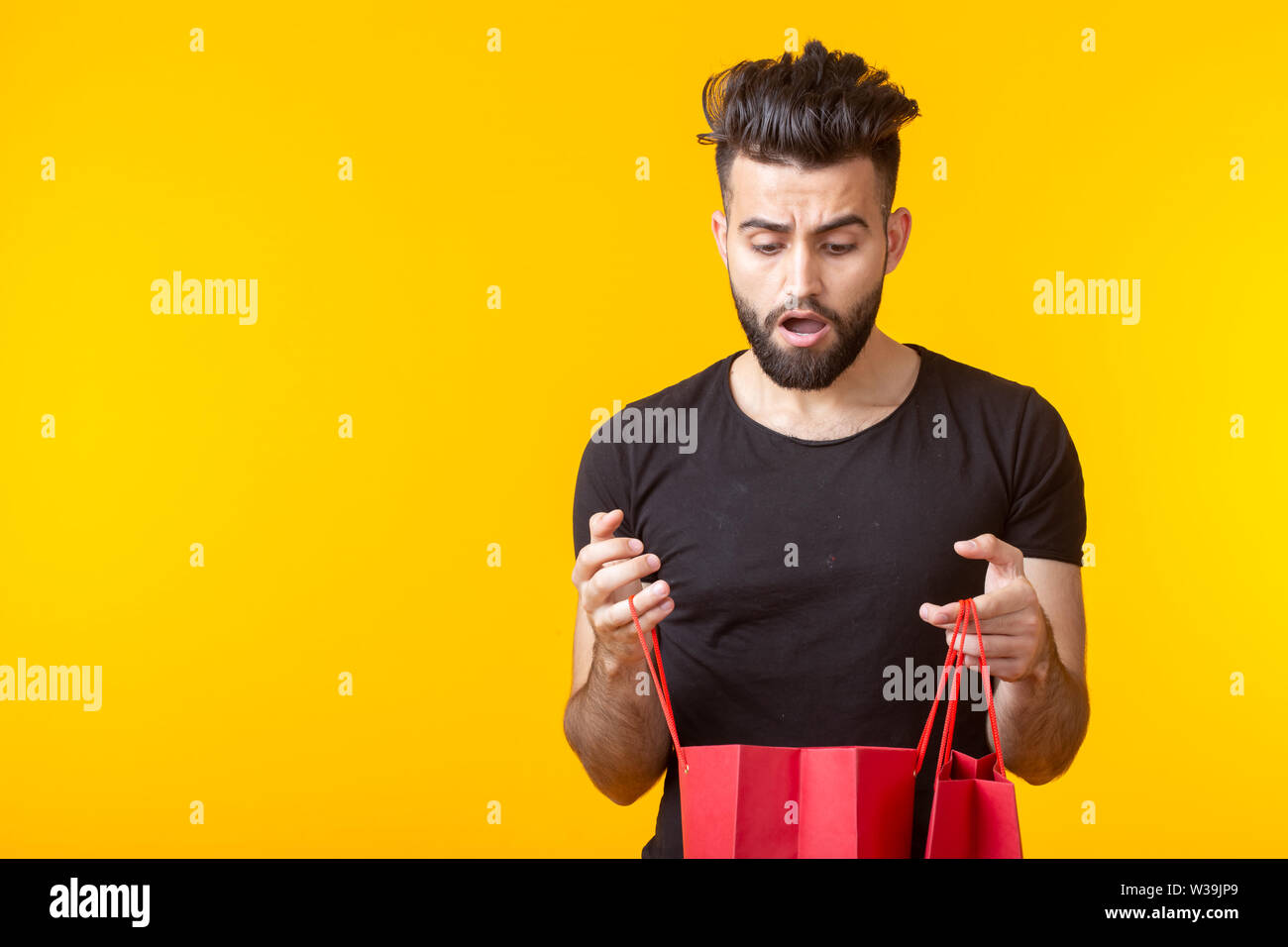 Cute young sad bearded man looks at the purchase in shopping bags on a ...