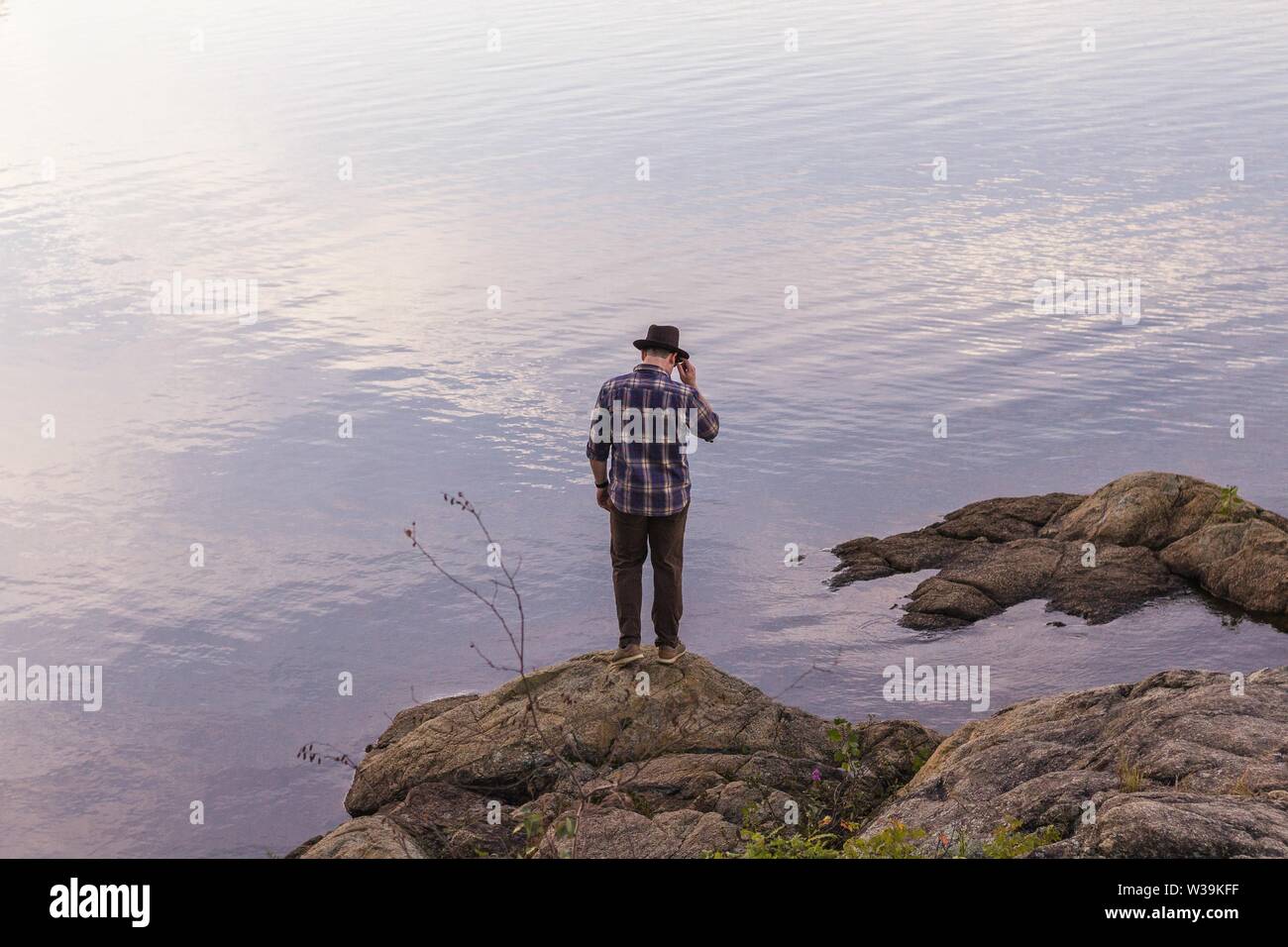 Male standing on a rock near a sea looking down Stock Photo - Alamy