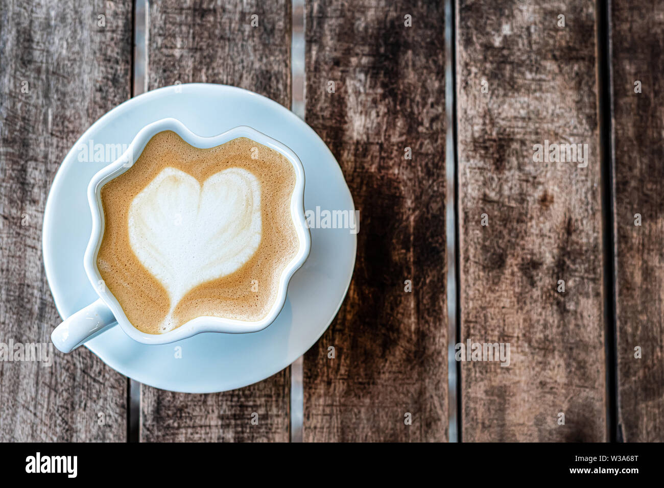 deformed mug of cappuccino coffee with a painted heart stands on a ...