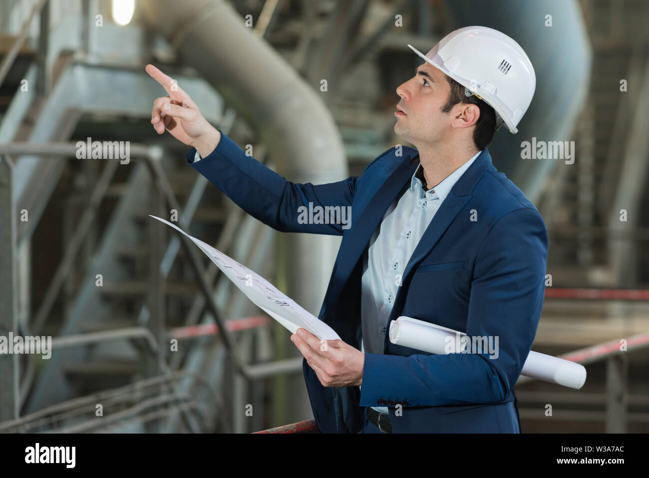 handsome engineer pointing at pipes in a factory Stock Photo - Alamy