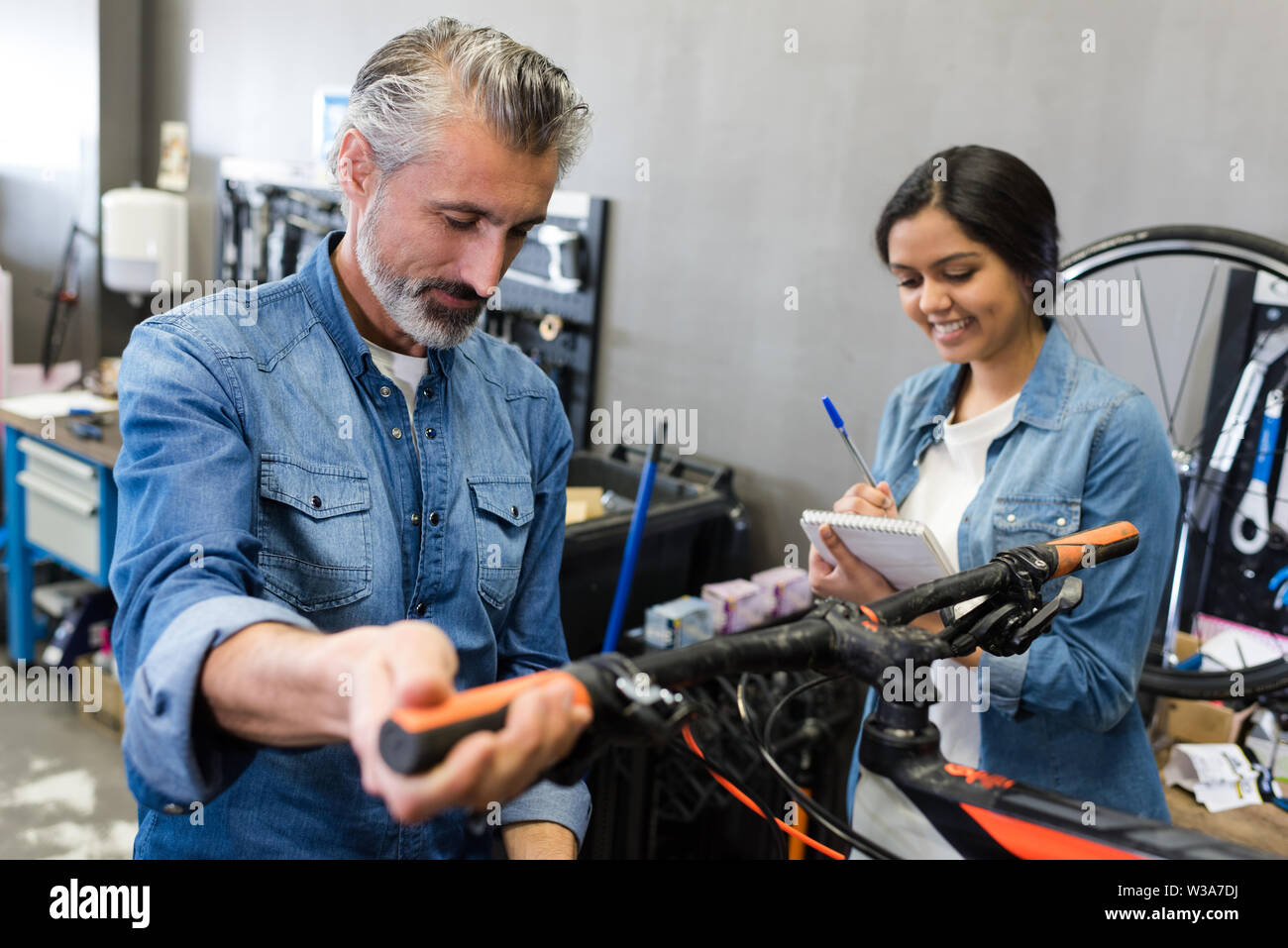 young apprentice making notes while mechanic works on bicycle Stock ...